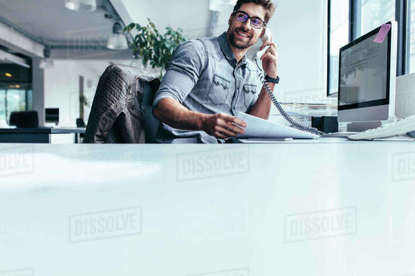 Businessman sitting in office and talking on telephone. Young man using ...