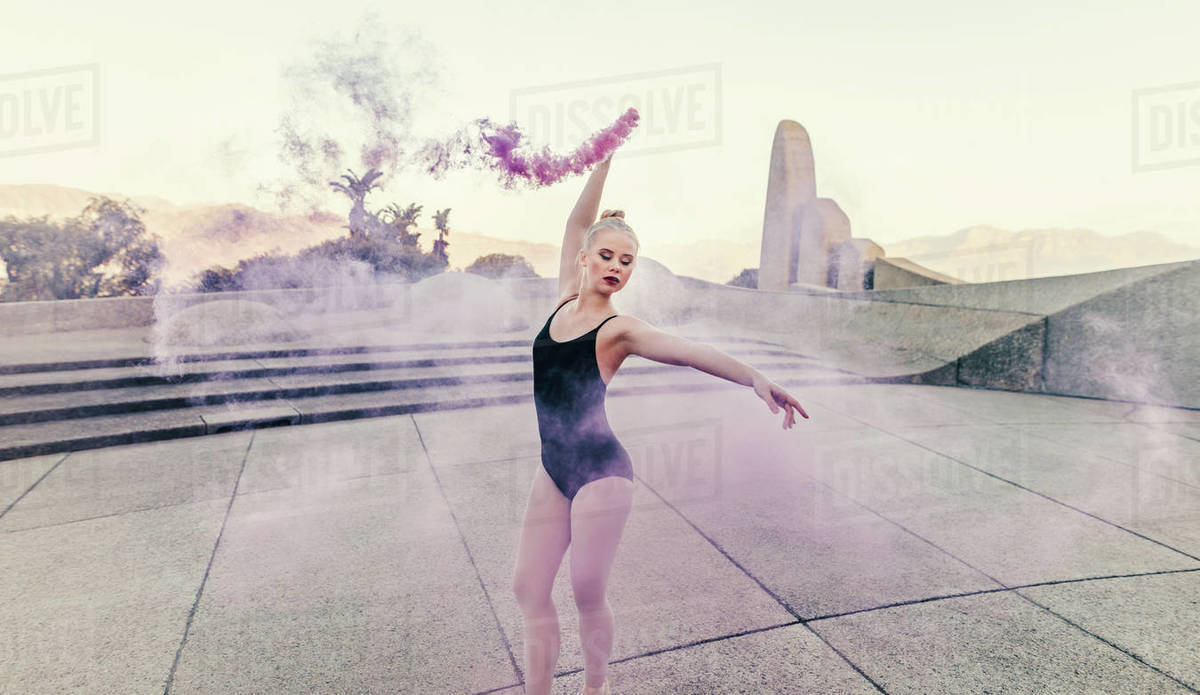 Ballet artist practicing dance moves outdoors using a pink smoke bomb ...