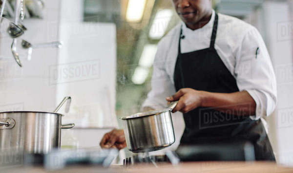 Cropped shot of chef putting cooking pot on stove. Chef cooking food at ...