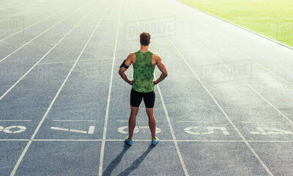 Rear view of an athlete standing on an all-weather running track ...