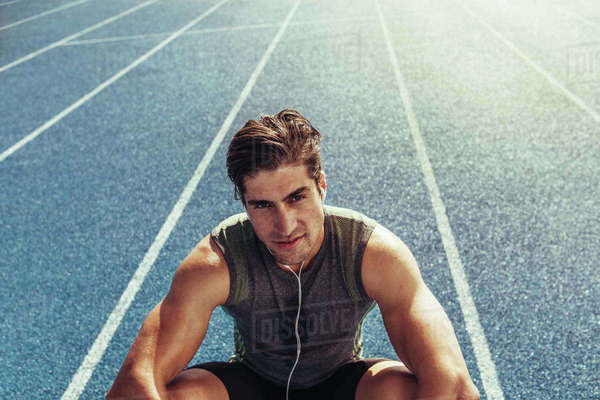 Close up of an athlete sitting on a running track listening to music ...