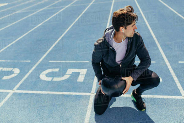 Athlete sitting on a running track near the start line with a medicine ...
