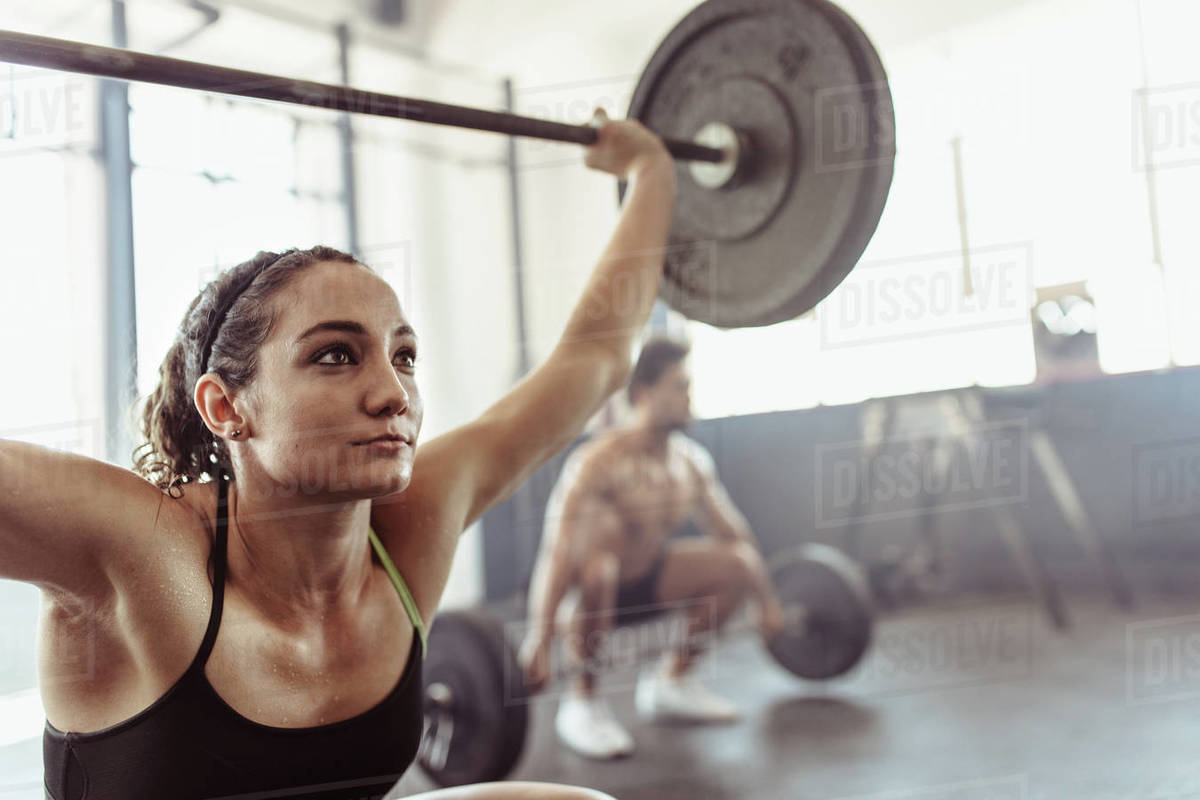 Tough young woman exercising with barbell. Determined female athlete ...