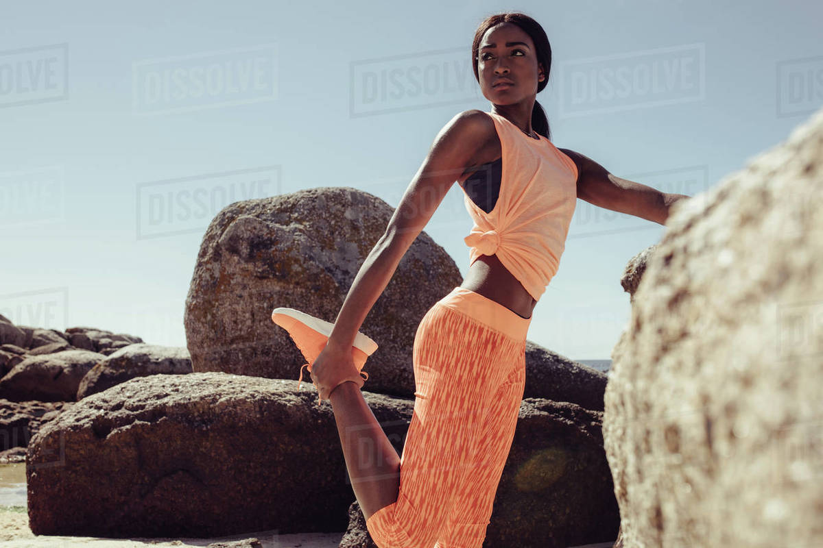 Healthy woman standing by a rock and stretching legs before running at ...