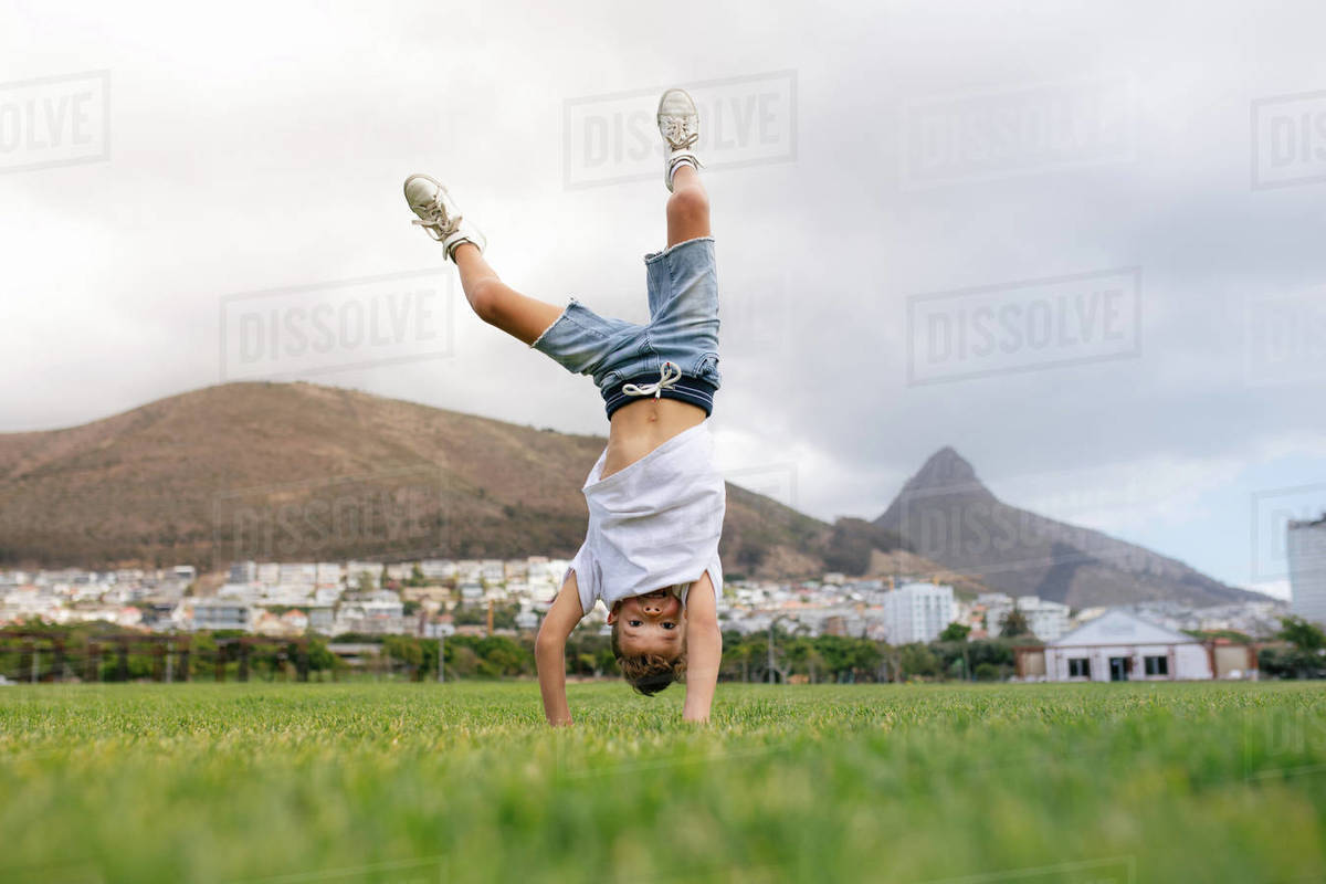 Boy balancing on hands in upside down position in a ground. Boy playing ...