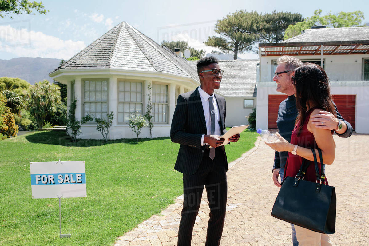 Real estate broker meeting and talking with clients outside a luxury ...