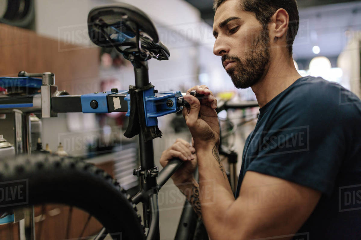 Worker repairing a bicycle at workshop. Man fixing a bicycle to a ...