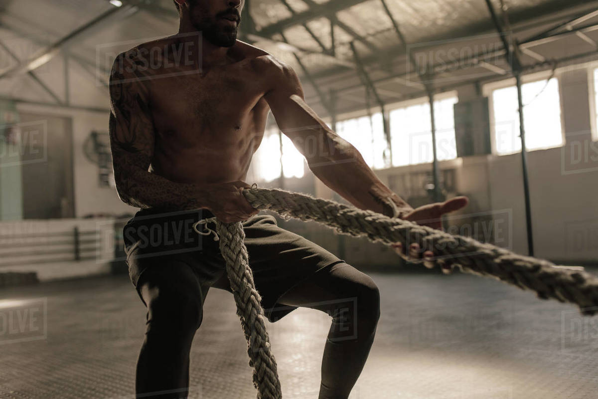 Male bodybuilder pulling rope at cross training gym. Male athlete doing ...