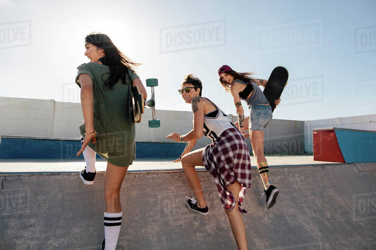 Happy female friends running over skateboard ramp. Group of female ...