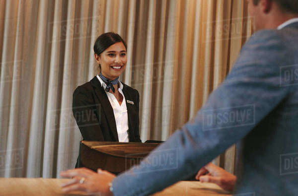 Female hotel receptionist attending a guest at reception counter. Happy ...