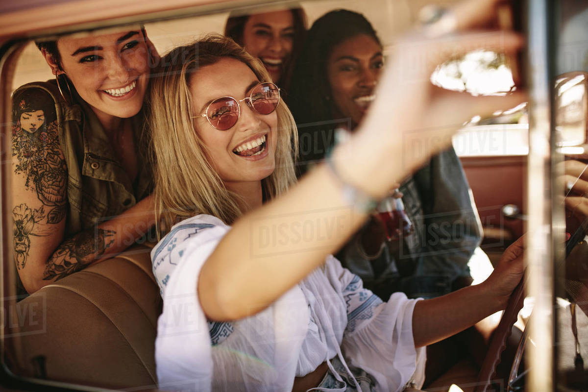 Group of young friends taking selfie in the car. Woman driving a car ...