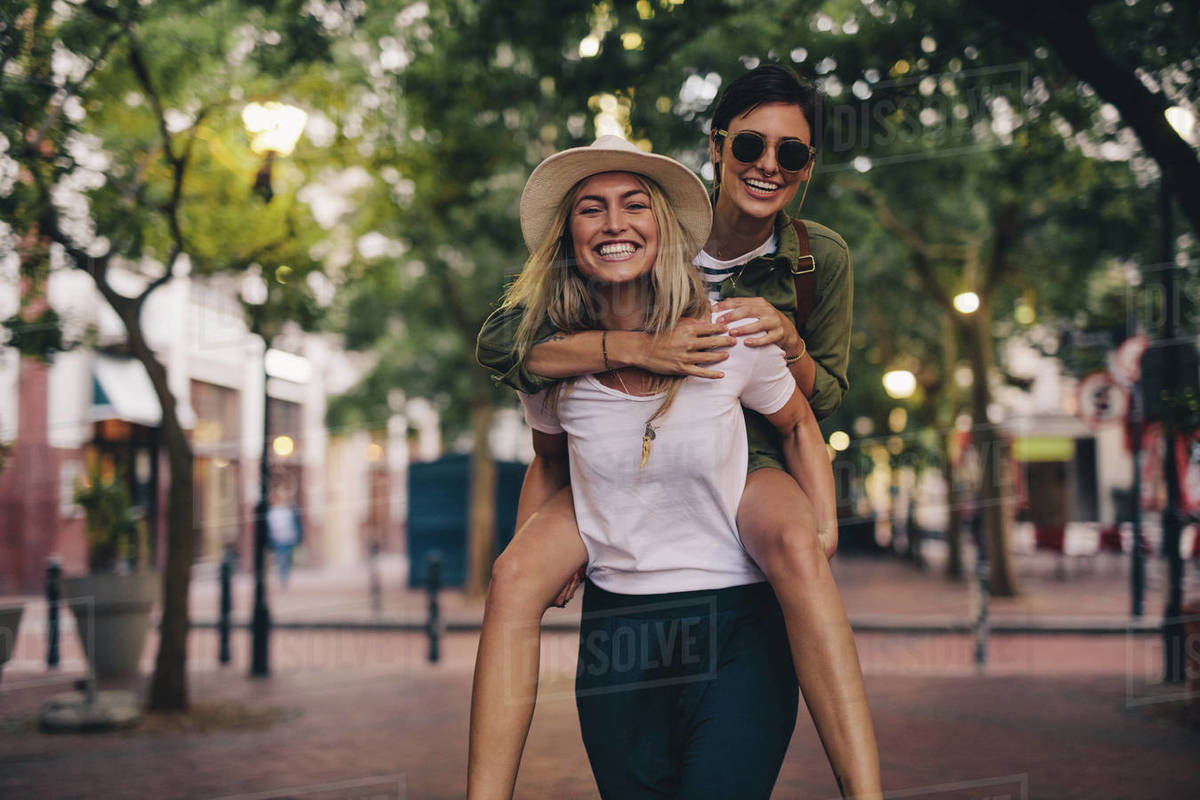 Beautiful young woman carrying her female friend on her back. Female ...