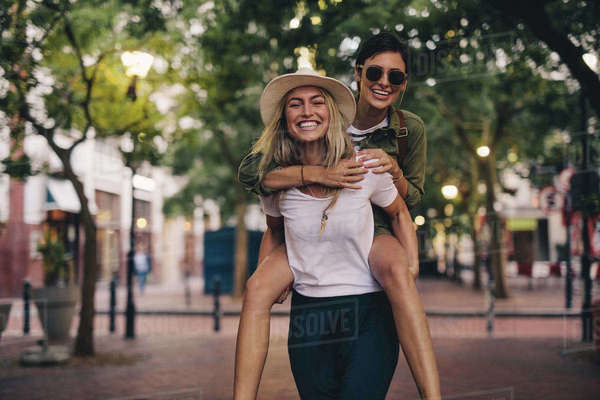 Beautiful young woman carrying her female friend on her back. Female ...