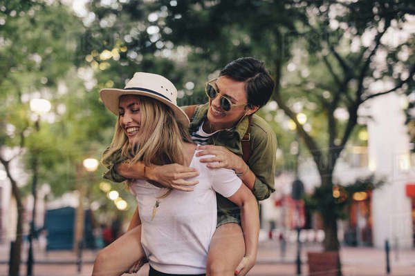 Woman carrying her female friend on her back and walking on the street ...