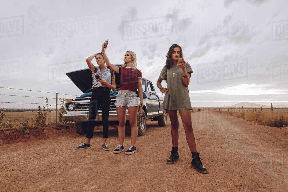 Three young woman stranded in middle of a countryside road with broken ...