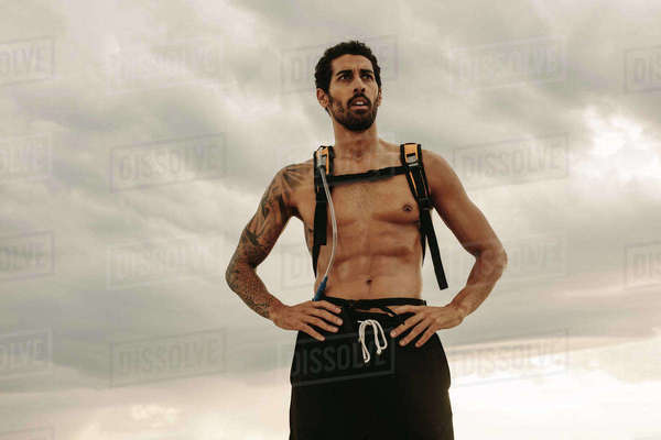 Strong and muscular man standing against cloudy sky and looking away ...