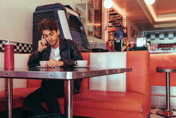 Man sitting at a diner with a coffee cups on the table talking over ...
