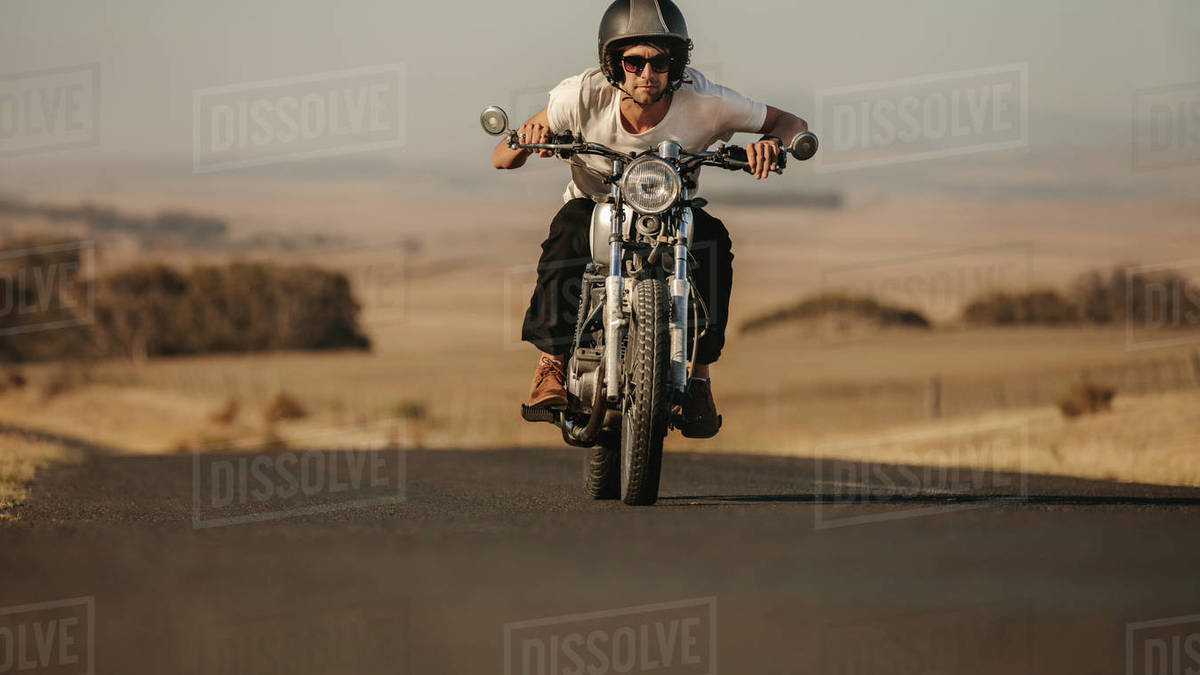 Portrait of young man driving a motor bike fast on country highway ...