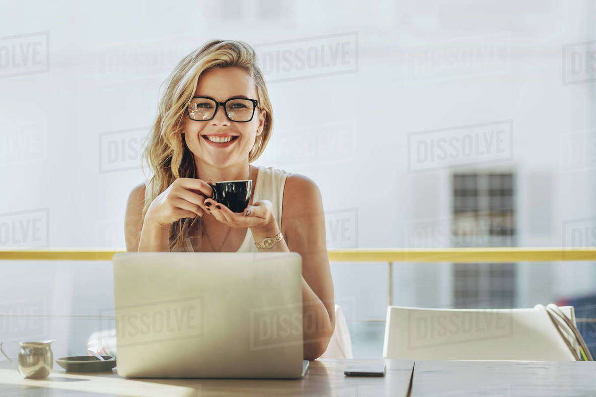Beautiful young businesswoman sitting at cafe with laptop holding a cup ...
