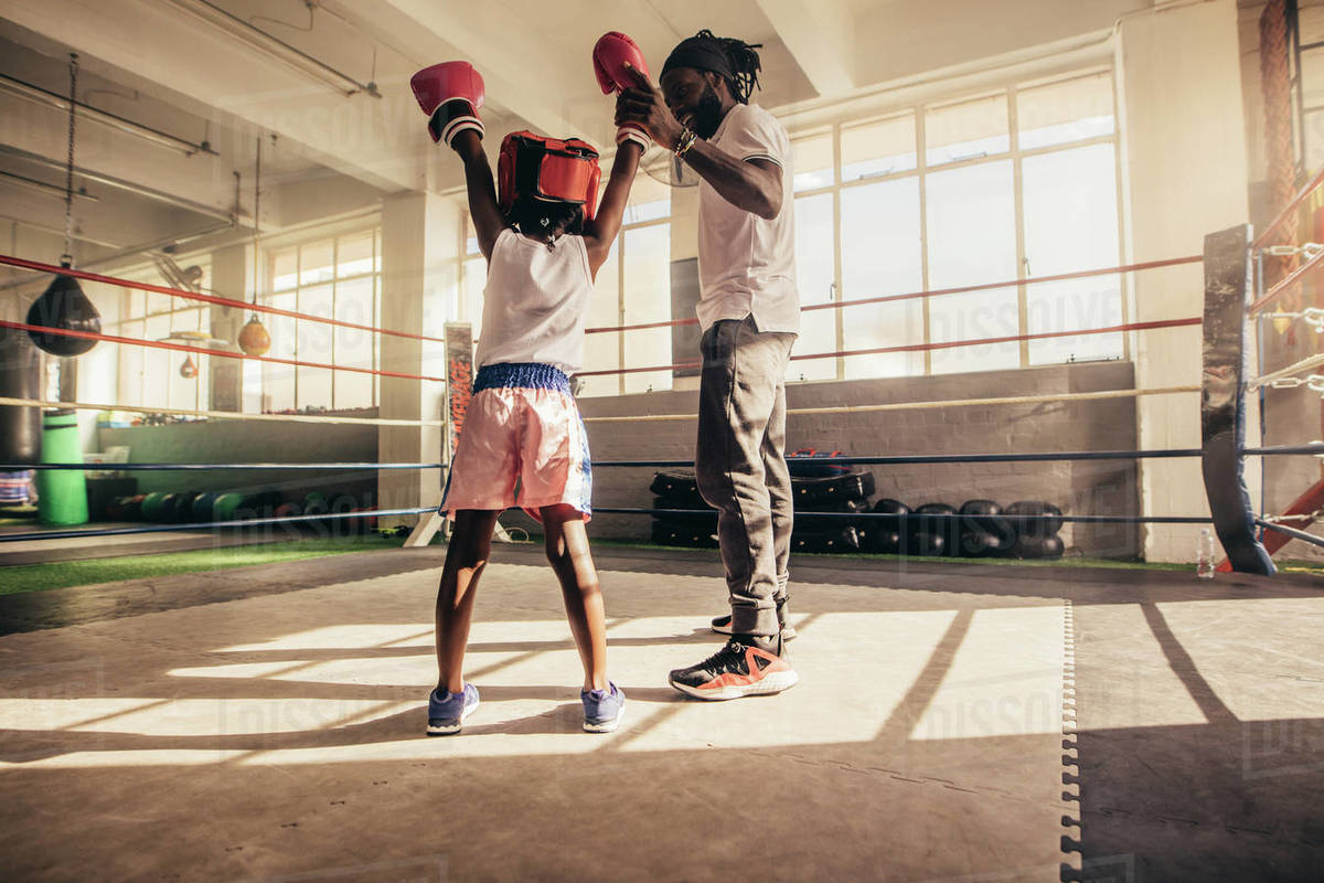 Rear view of a kid standing inside a boxing ring with raised hands ...