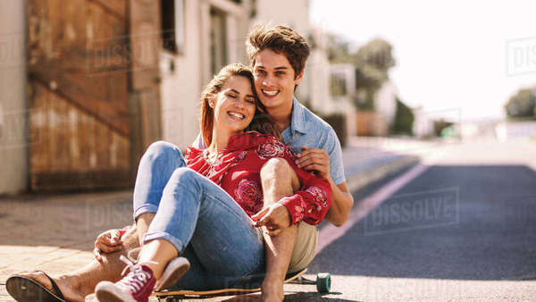 Happy couple sitting together on a skateboard rolling down an empty ...