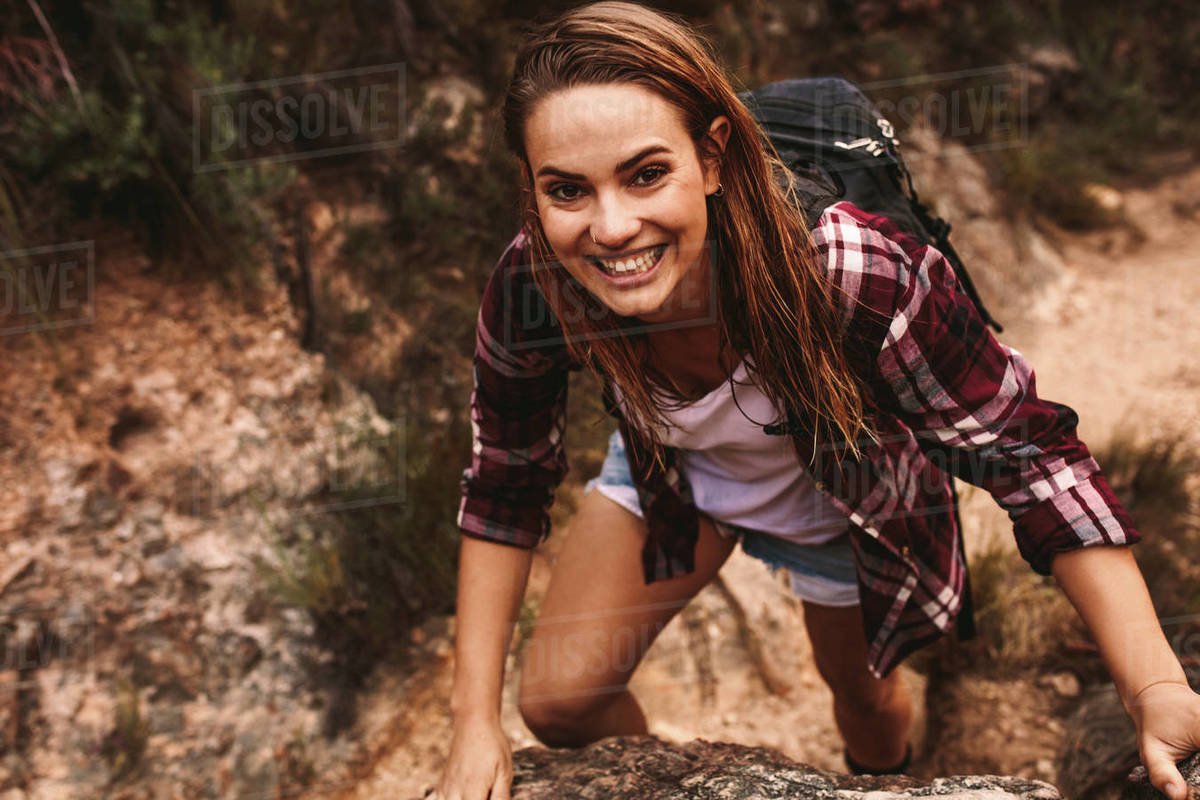 Portrait of woman hiker climbing a rock and looking at camera smiling ...