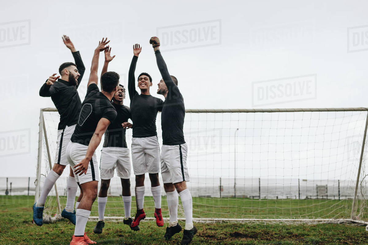 Excited football players jumping in excitement standing in a huddle ...