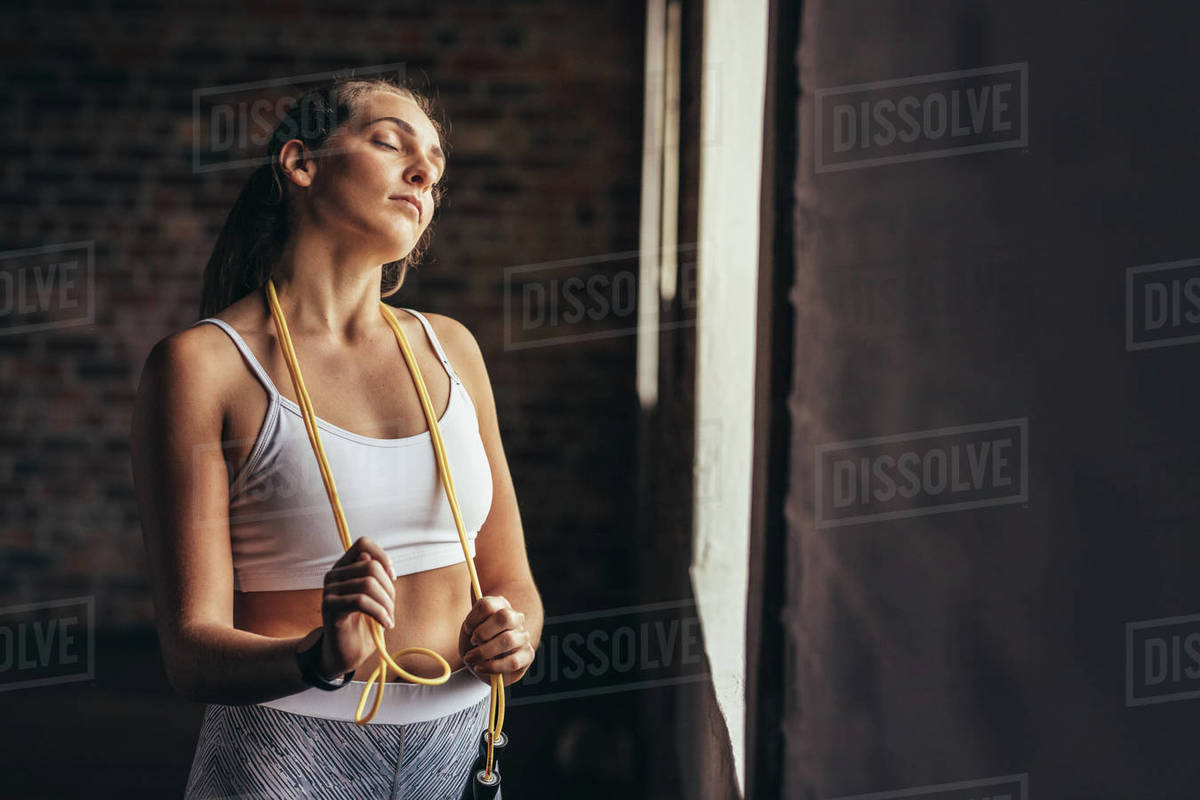 Woman athlete with skipping ropes around her neck standing by gym ...