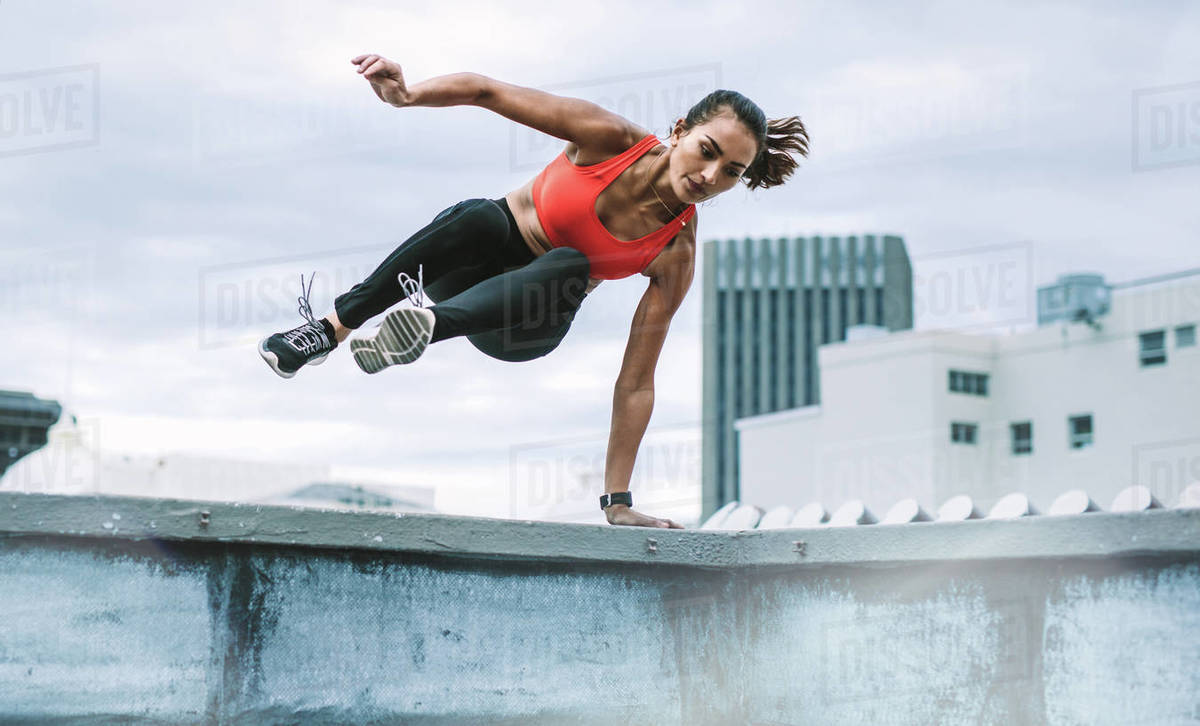 Female athlete jumping on to the rooftop from the roof fence taking ...