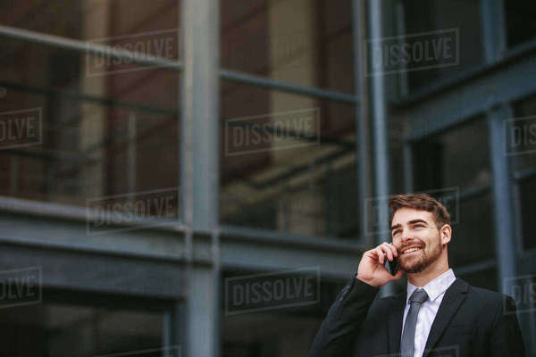 Positive young businessman making a phone call outdoors with office ...
