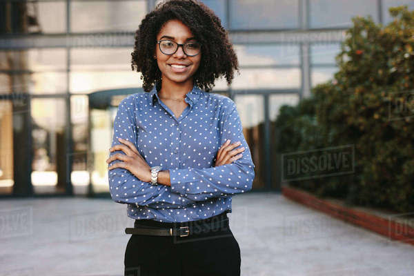 Portrait of positive young african woman standing outside with her arms ...