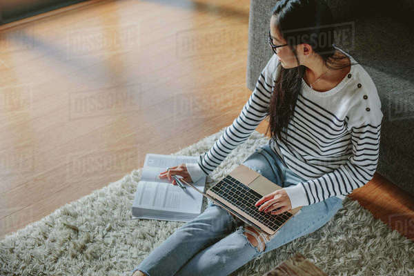 Top view of woman sitting on floor and studying with book and laptop ...