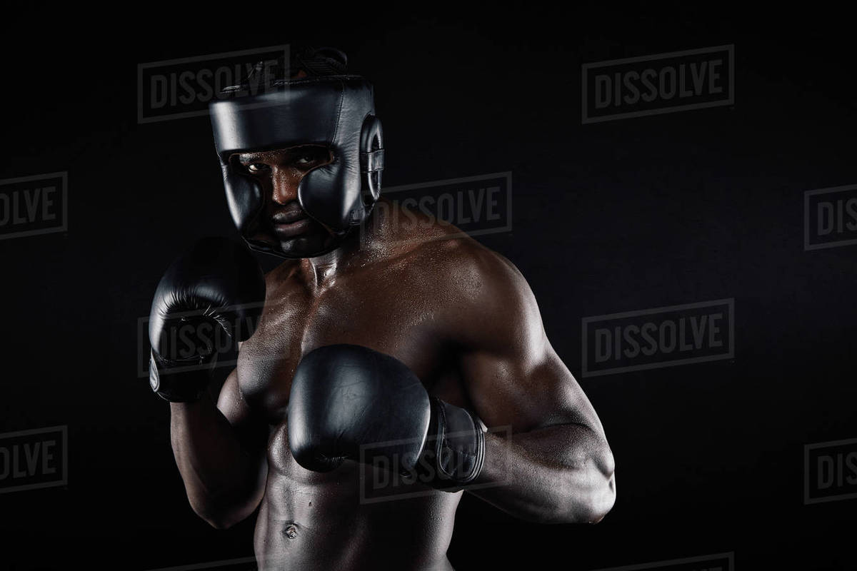Portrait of a young male boxer in a fighting stance against black ...
