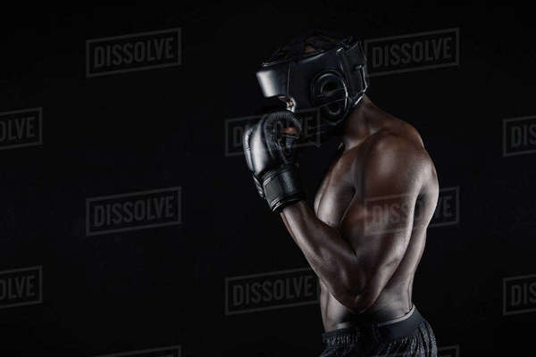 Side view of a young male boxer in a fighting stance on black ...