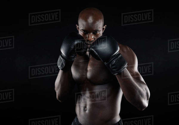 Portrait of tough male boxer posing in boxing stance against black ...
