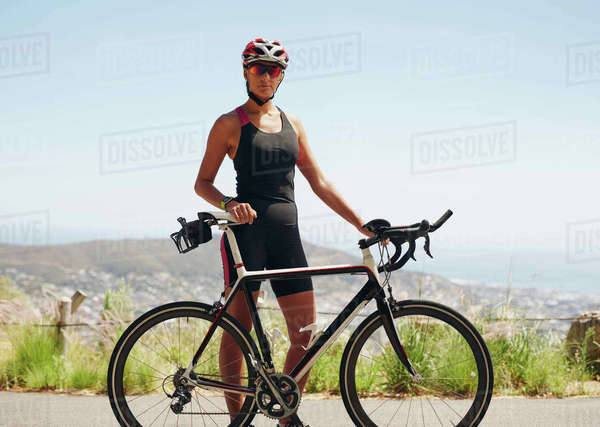 Portrait of confident young female cyclist standing with her bicycle on ...