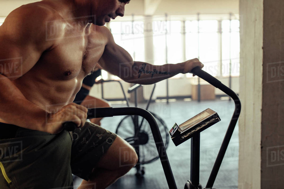 Cropped shot of muscular man at the gym riding on the spinning bike ...