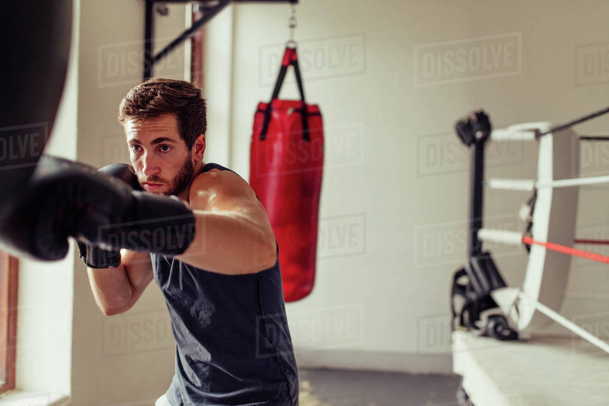 Young boxer with beard strikes punching bag in exercise gym near boxing ...