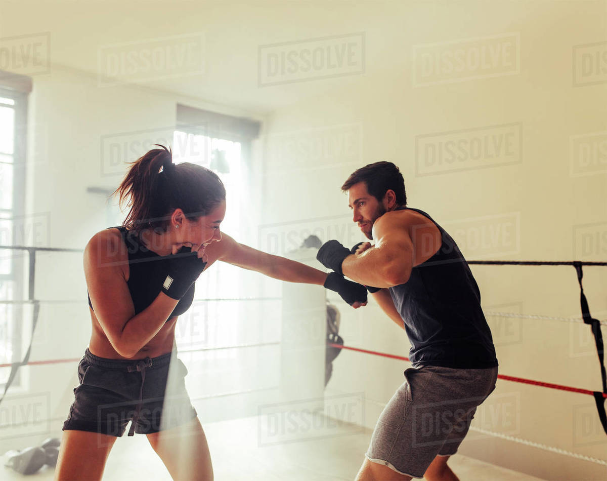 Male and female athletes sparring in boxing ring as sunshine pours in ...