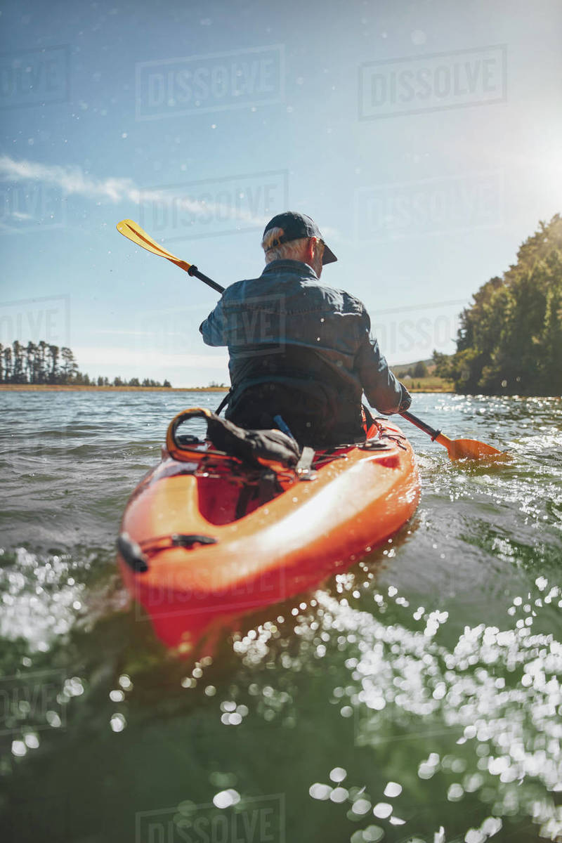 Rear view image of a mature man canoeing in a lake. Senior man paddling ...