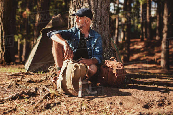 Portrait of senior man sitting under a tree with a backpack. Mature man ...