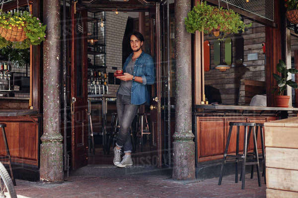 Full length portrait of relaxed young male standing at the entrance of ...