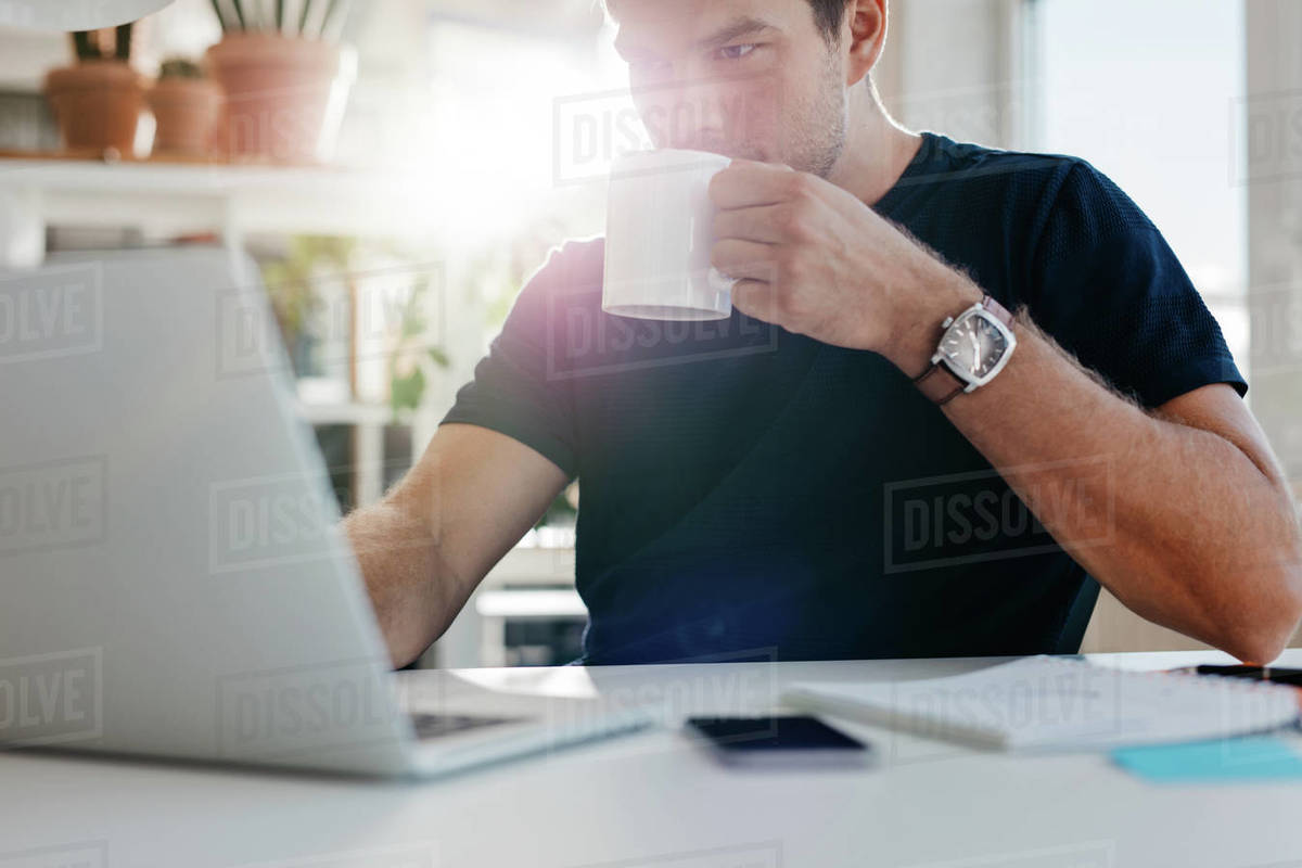 Image of young businessman with cup of coffee looking at laptop screen ...