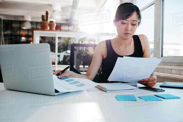 Portrait of young asian woman reading documents at her desk ...