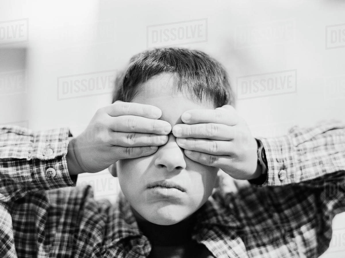 Close up of boy holding hands over eyes - Stock Photo - Dissolve