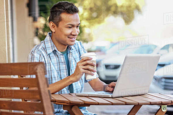 Malaysian man drinking coffee and using laptop at cafe - Royalty-free ...