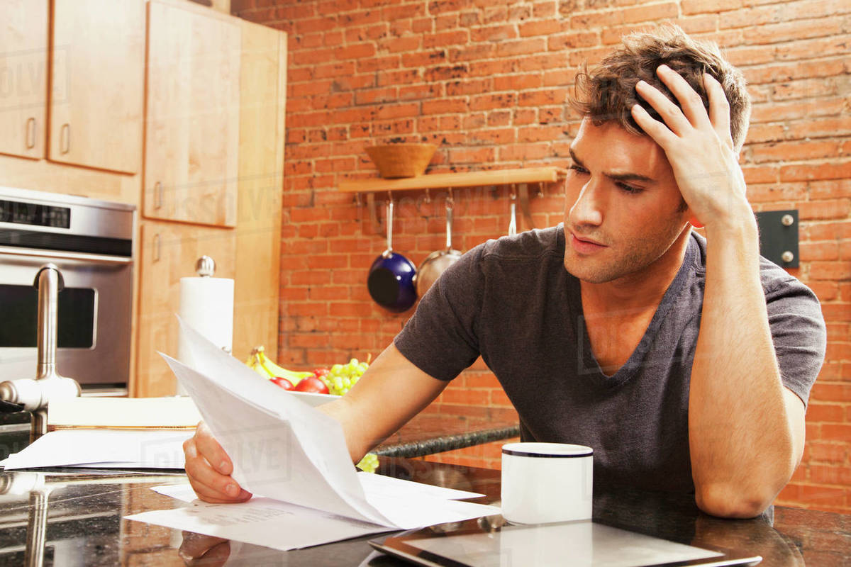Caucasian man looking at paperwork in kitchen - Stock Photo - Dissolve