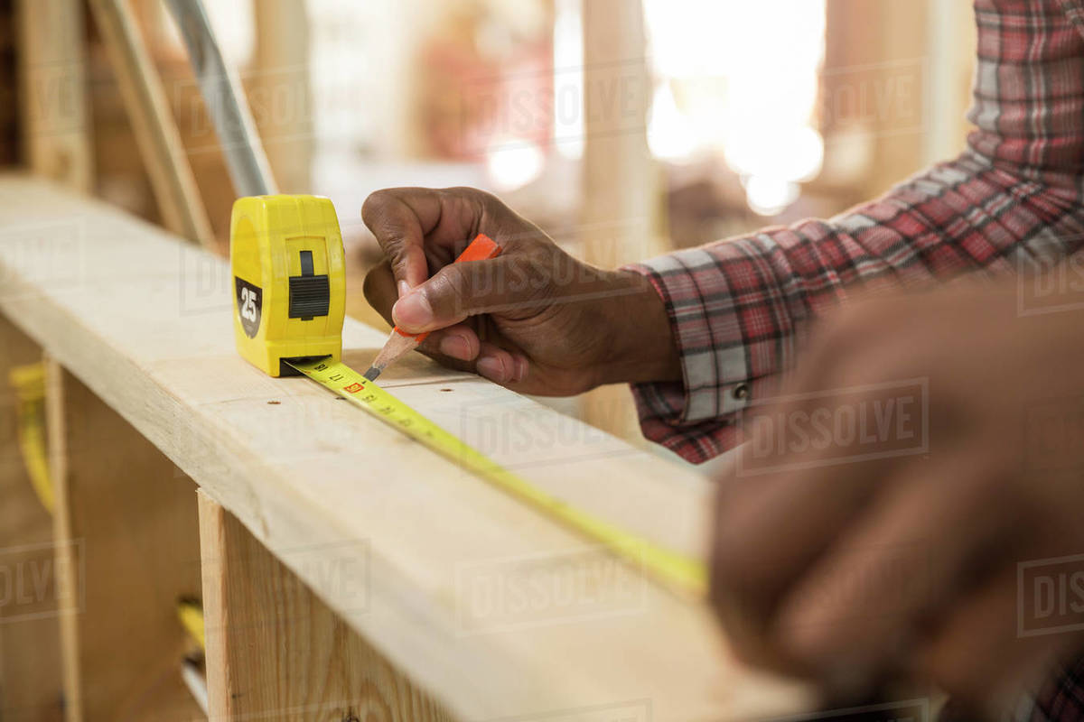 Worker measuring wood at construction site - Stock Photo - Dissolve