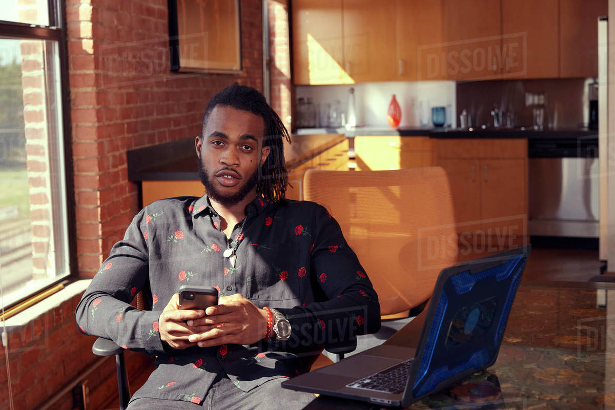 Portrait of young ethnic man sitting at conference table using ...