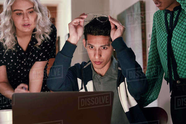 Group of young co-workers gathered around laptop computer looking at ...